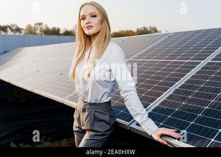 Blonde model with solar panels stands in row on the ground. Girl ...