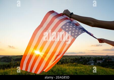 Human hands holding waving american national flag in field at sunset ...