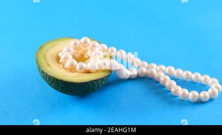 Half fresh avocado fruit with pearls on blue background. Fashionable ...