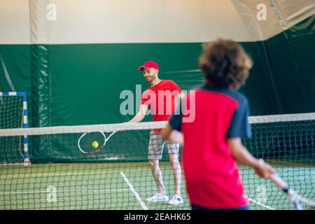 Coach in a red cap and a boy with a tennis racket Stock Photo - Alamy