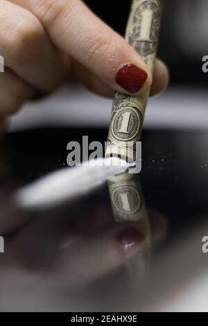 A young woman snorting a line of cocaine off a mirror through a rolled ...
