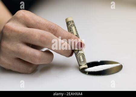 A young woman snorting a line of cocaine off a mirror through a rolled ...