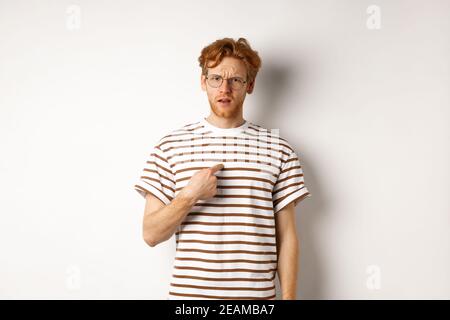 Confused redhead man in glasses pointing at himself, looking questioned ...