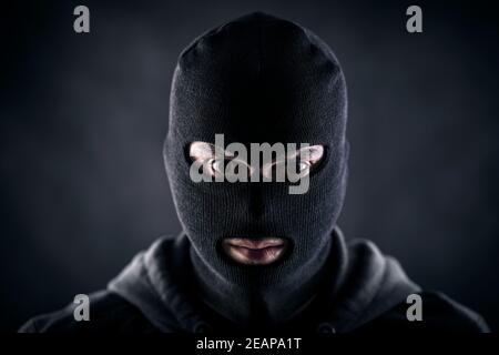 Portrait of dangerous bandit in black wearing balaclava and holding gun ...