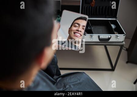 Handsome male in black peignoir resting while getting hairdressing in ...