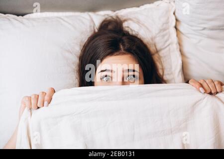Scared girl hiding under blanket. Startled kid sitting in bed on night ...