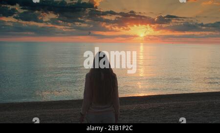 Medium shot of admiring sunrise on seashore woman raising up her hands ...