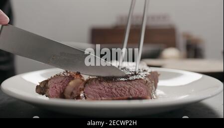 man slicing new york steak on white plate, wide photo Stock Photo - Alamy