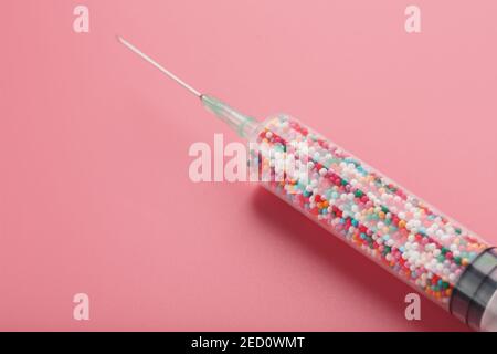 Medical Syringe filled with colorful balloons on a pink background with ...