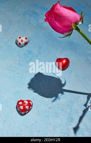 Purple rose with hard shadow and three heart-shaped candies on a light ...