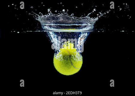 Tennis ball falling in water with a splash against dark background ...