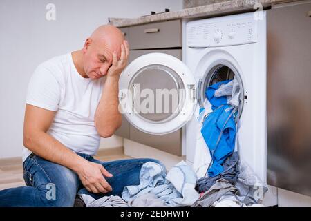 tired bald man sitting with dirty laundry in the washing machine ...