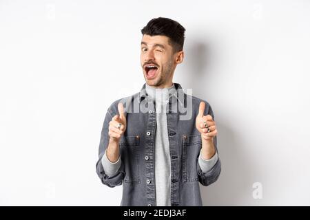 Funny handsome guy winking and pointing fingers at camera, inviting you ...