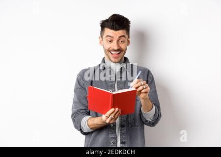 Excited guy writing in planner and smiling, writing down ideas in ...