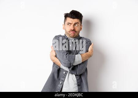 Displeased young man feeling discomfort, hugging himself and staring ...