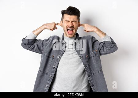 Annoyed guy shut ears and screaming, displeased by loud noise, yelling ...