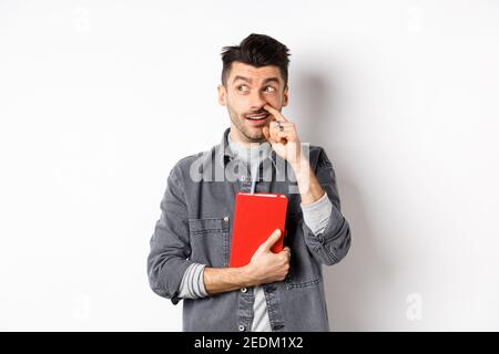 Guy picking nose and look aside at logo, holding red book or planner in ...
