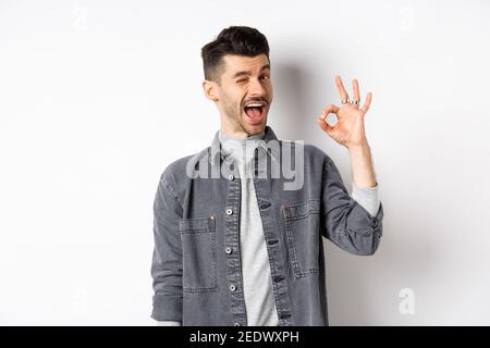 Excited handsome guy with moustache, winking and showing okay sign ...