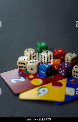 Colourful dice lie on colourful playing cards against a dark, neutral ...