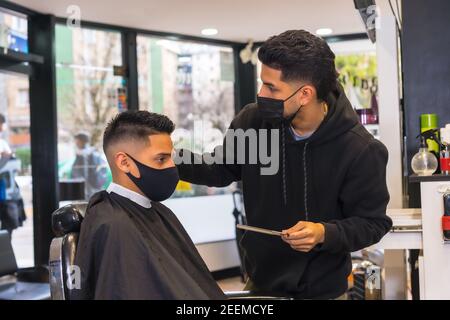 Young male hairdresser in mask cuts hair of girl in mask at beauty ...