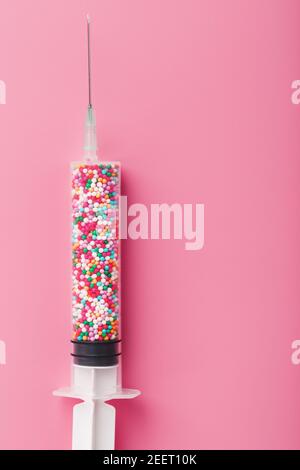 Medical Syringe filled with colorful balloons on a pink background with ...
