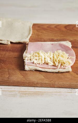 Vertical shot of raw toast rolls with ham and grated cheese on a board ...
