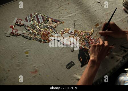 Craftsman colours a wayang kulit puppet of King Kresna (Krishna) in the ...