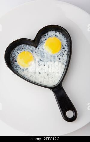 Two heart-shaped fried eggs on a black ceramic plate on a dark concrete ...