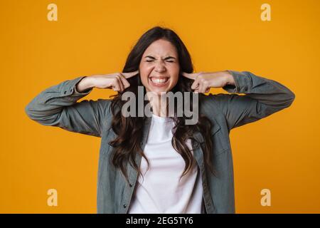 Unhappy beautiful girl plugging her ears while posing at camera ...