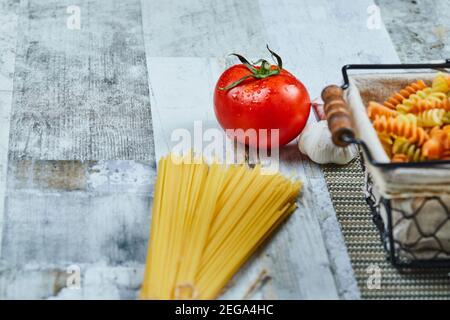 Basket of colorful uncooked pasta, spaghetti and vegetables on a blue ...