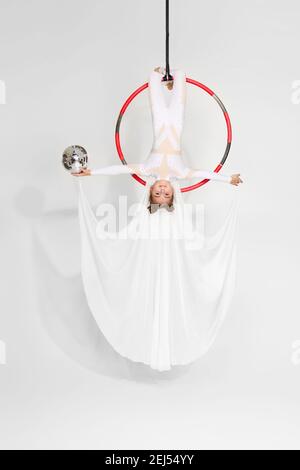 Little acrobat girl shows an acrobatic performance on an aerial hoop ...