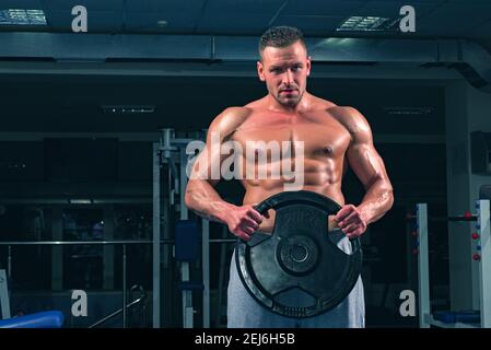 Powerlifter with weight disk in sport gym. Bodybuilder with heavy disk ...