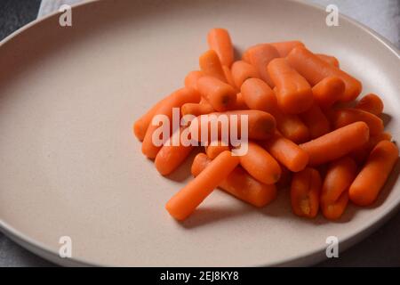 Bunch of cooked small boiled carrots and broccoli on white plate ...