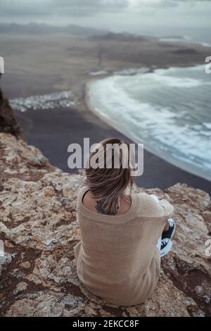 Serene female explorer sitting on roof of van and enjoying summer ...