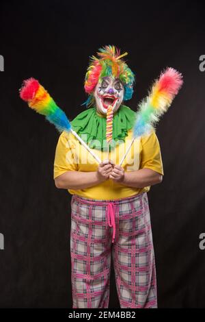 Scary clown with colorful mohawk and a smile with a lollipop on a black ...