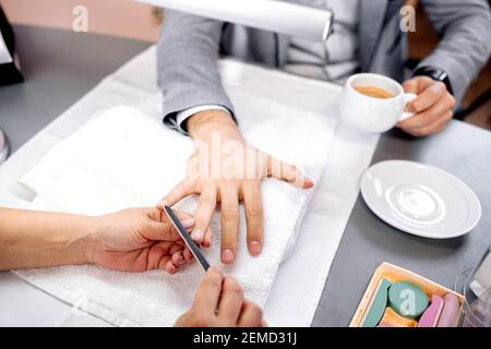 Trimming and smoothing the edges of nails on a young man’s hand ...
