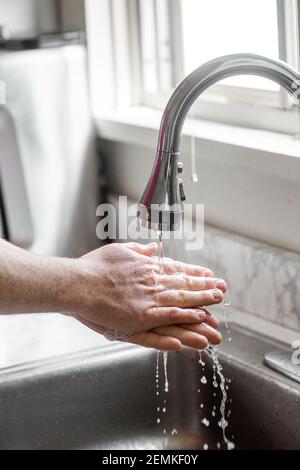 Man washing hands in modern silver kitchen sink under running water ...