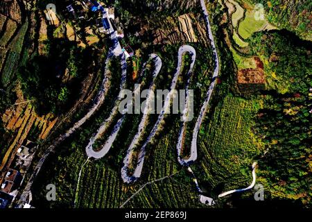 An aerial view of a zigzag highway connecting remote and poor villages locating among mountains ...
