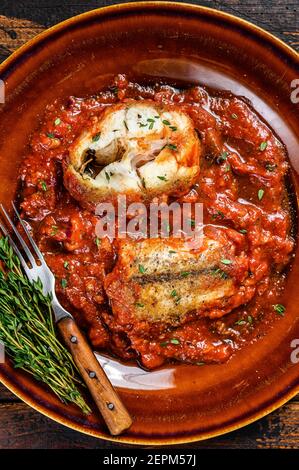 Roast grenadier white fish fillet with tomato sauce in a plate. Dark ...