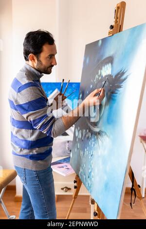 Young hispanic man with beard painting on canvas at home looking ...