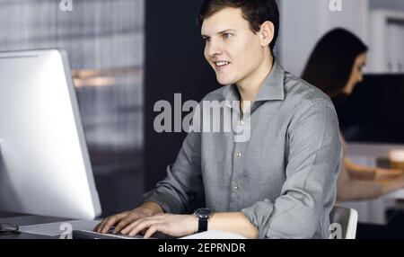 Dark-haired young businessman and programmer in a green shirt is ...