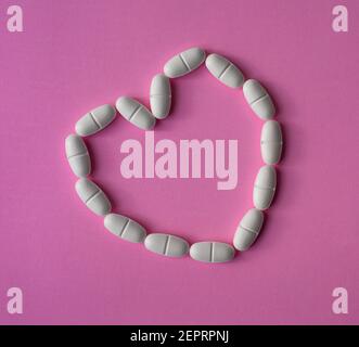 Pink tablets are arranged in a heart shape isolated on white background ...
