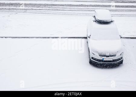 A car is parked on a snow-covered road surrounded by trees and winter ...