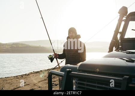 Young fisherman standing near his car and holding fishing equipment ...