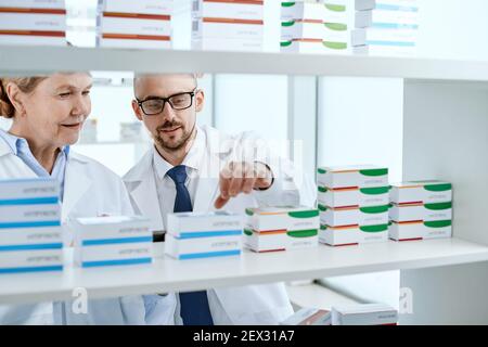 Pharmacist with female assistant in pharmacy standing in front of shelf ...