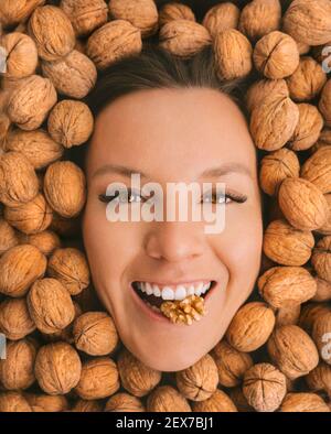 Woman smiling face on a walnuts background. Eating nuts. Strong teeth ...