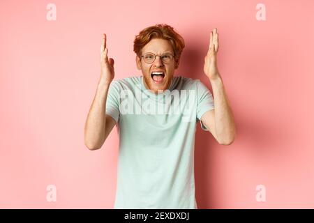 Angry redhead guy in glasses shouting, frowning and shaking hands with ...