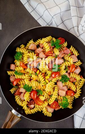 Colorful pasta rotini, cherry tomatoes and ham on pan. Close up. Top ...