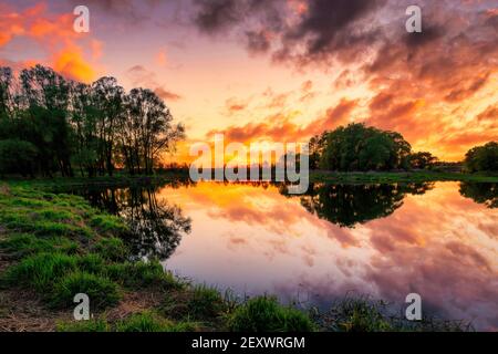 River with cloudy skies and willows growing along the shore in spring ...