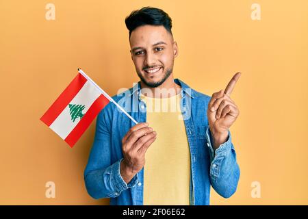 Young arab man holding lebanon flag doing ok sign with fingers, smiling ...